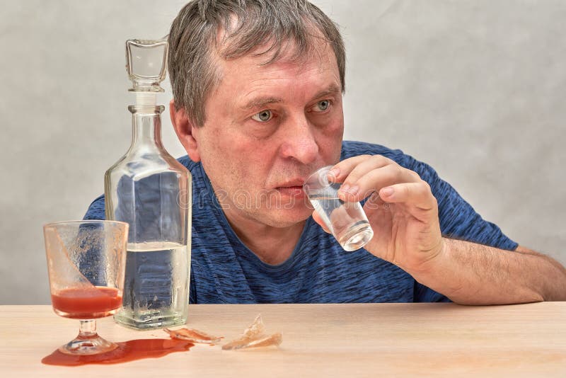 A Sad Man Sits at the Table and Drinks Vodka from a Glass with Alcohol ...