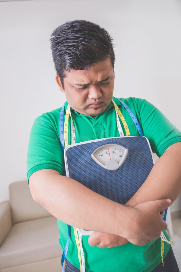 Sad Obese Man Holding a Weight Scale, Thinking about His Weight Stock ...