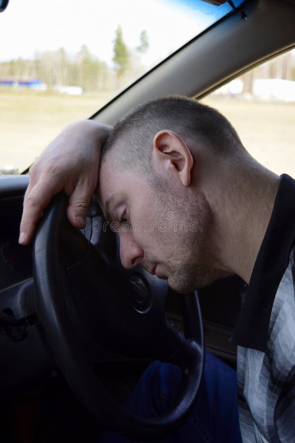A Sad Young Man is Sitting in the Car, Leaning on the Steering Wheel ...