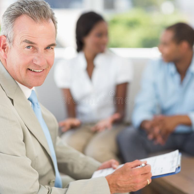 Salesman Smiling at Camera with Couple Behind Him Stock Photo - Image ...