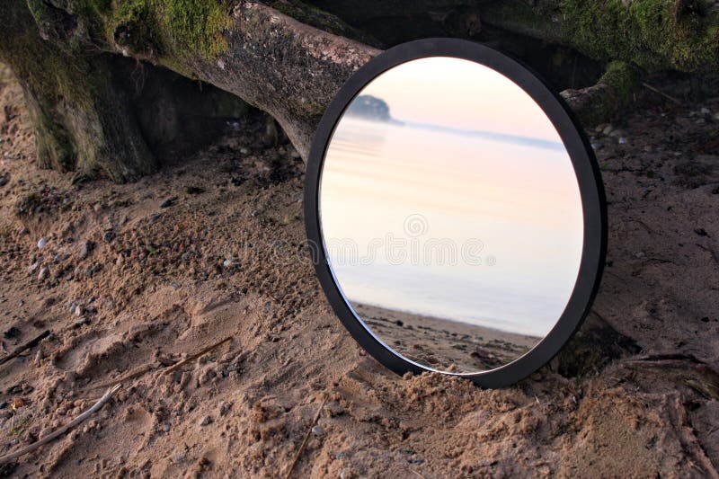Sand on the Beach and a Round Black Mirror with a Reflection of the Sea ...