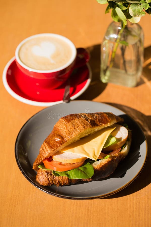 A Sandwich with Ham, Tomato, and Cheese Sits on a Plate Next To a Cup ...