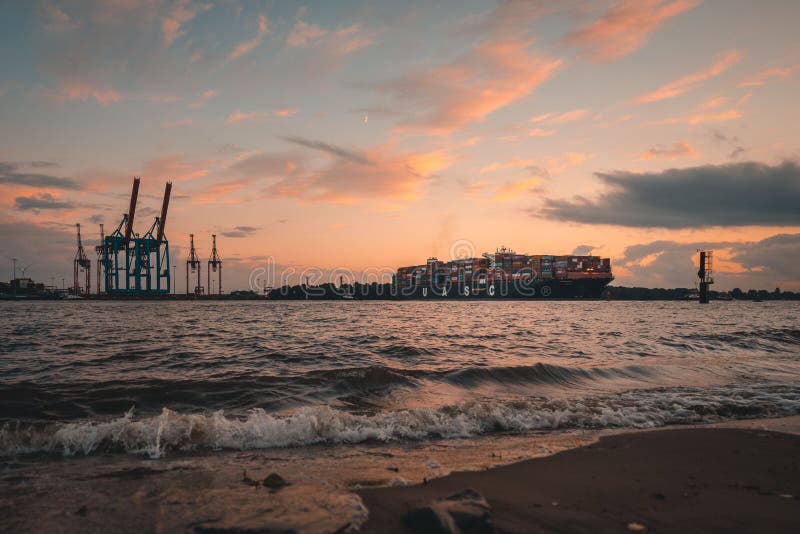 Sandy Beach with Cargo Ships and Cranes in the Background at Sunset ...
