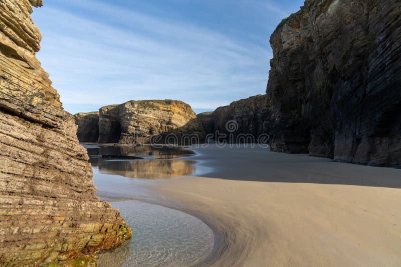 Sandy Beach with Tidal Pools and Jagged Broken Cliffs Behind in Warm ...