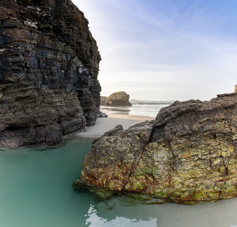 Sandy Beach with Tidal Pools and Jagged Broken Cliffs Behind in Warm ...