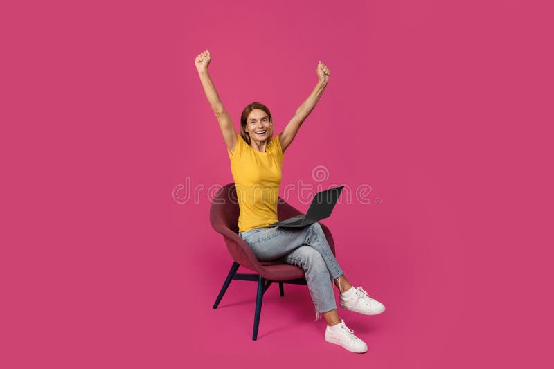Satisfied Adult European Woman Sitting On Chair With Laptop Raising