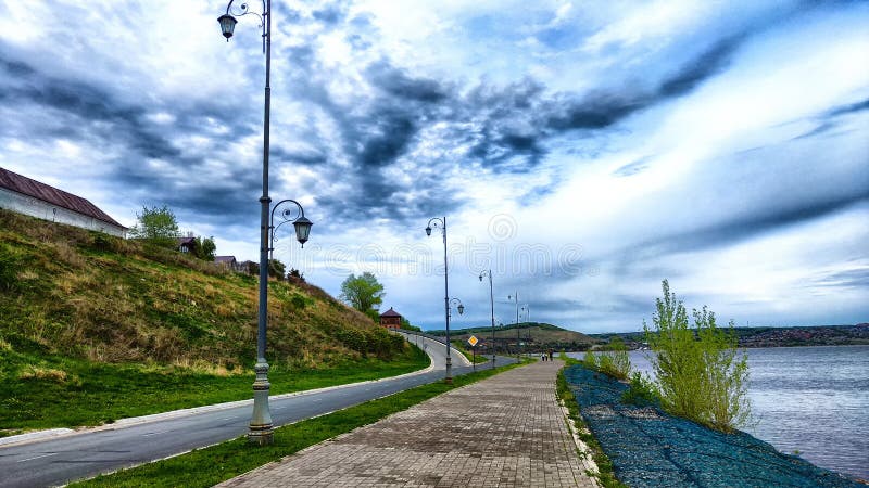 Scenic Riverside Walkway with Lamp Posts and Dramatic Clouds in Early ...