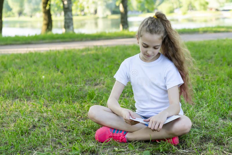 A School-age Girl Reading a Book Sitting on the Grass in the Park Stock ...