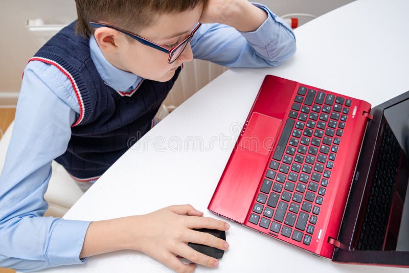 A School Boy Sitting by the Table with a Laptop and Doing Homework, E ...