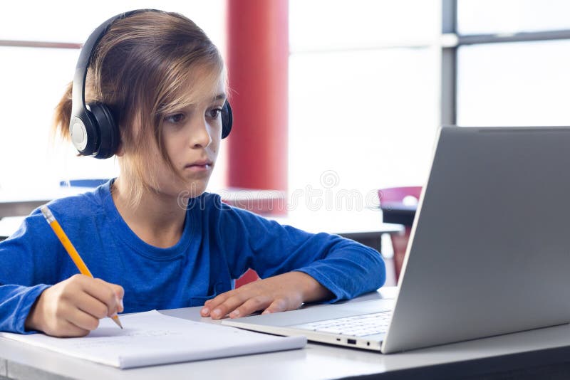 In School, Boy Wearing Headphones Writing in Notebook while Using ...