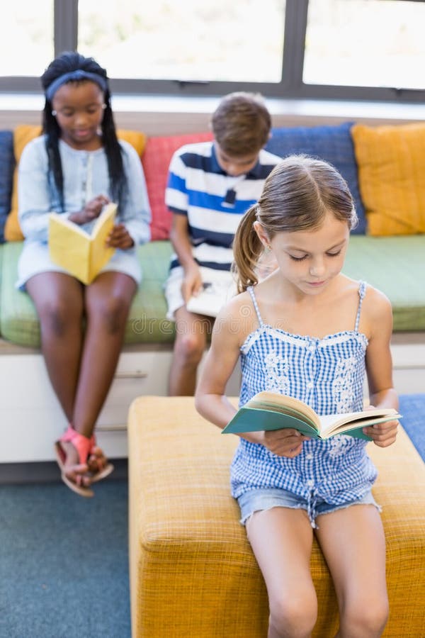 School Kids Sitting on Sofa and Reading Book in Library Stock Photo ...