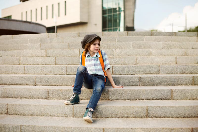 A Schoolboy with a Paunch on His Shoulders and a Cap Sits on the Steps ...