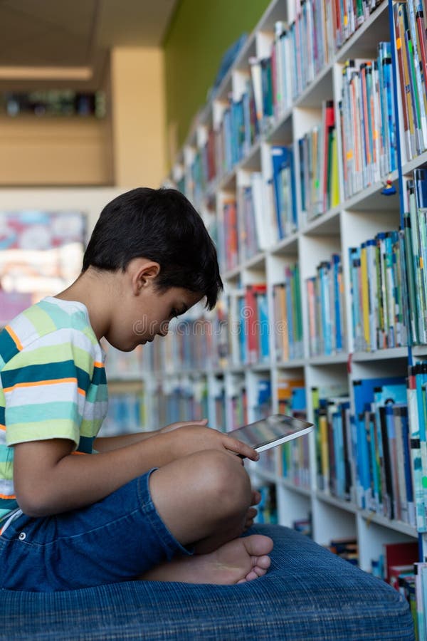 Schoolboy Using Digital Tablet on Sofa in Library Stock Photo - Image ...