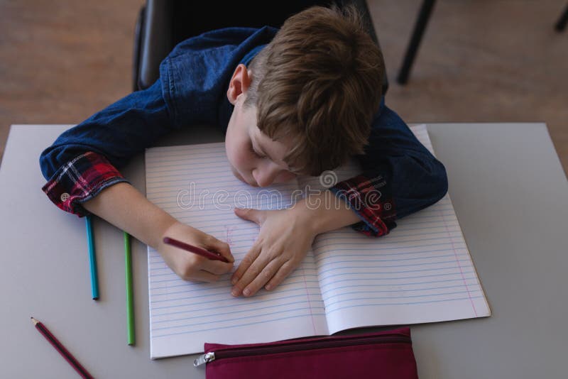 Schoolboy Writing on Notebook and Sitting at Desk in Classroom Stock ...
