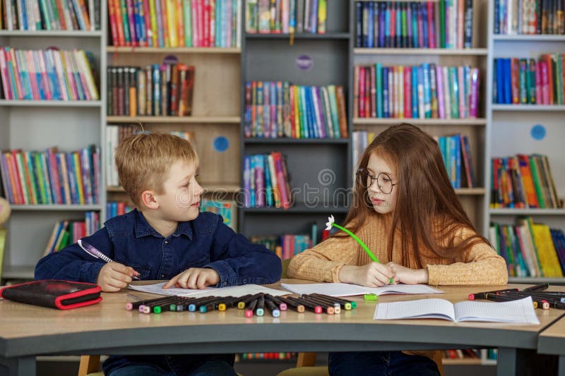 Two Schoolchildren Write and Draw Sitting at Table in Library ...