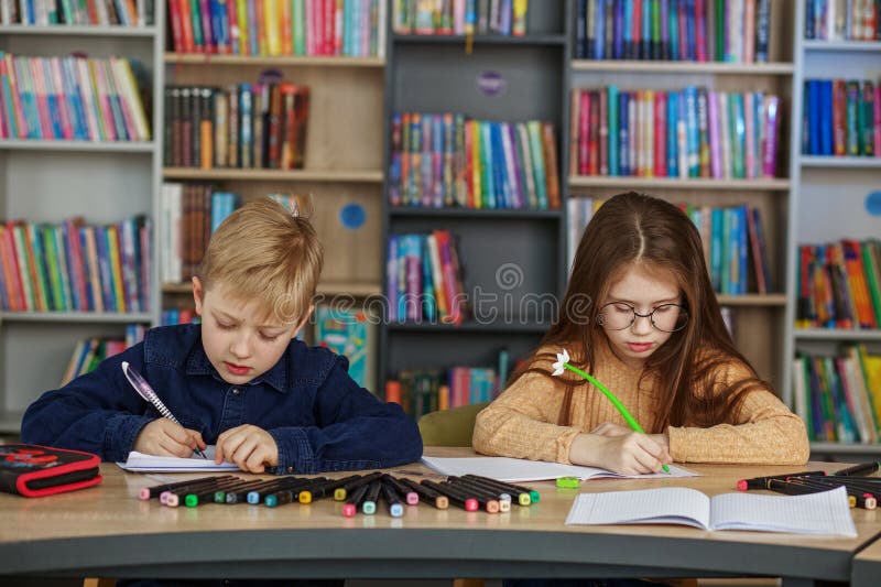 Two Schoolchildren Write and Draw Sitting at Table in Library ...
