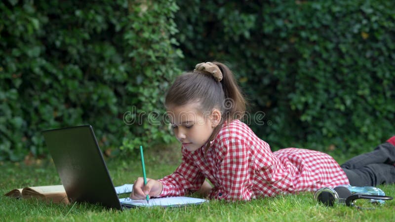A Schoolgirl Lying on the Grass with a Laptop Does Her Homework Online ...