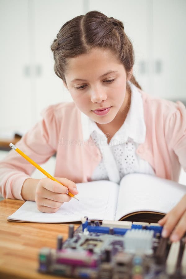 Female Teenage Student Writing in Open Notebook and Examining Circuit ...