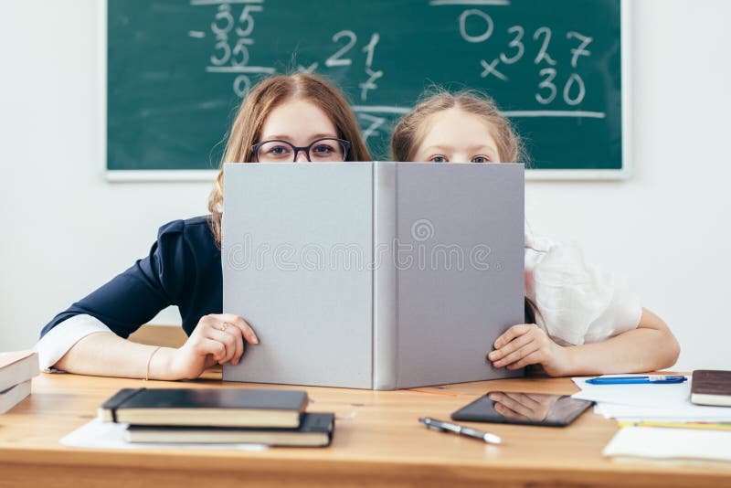 Schoolgirls Hiding Behind Book Sitting in a Classroom Stock Image ...