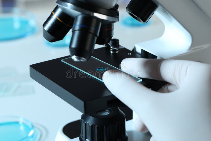 Scientist Examining Sample of Light Blue Liquid on Slide Under ...