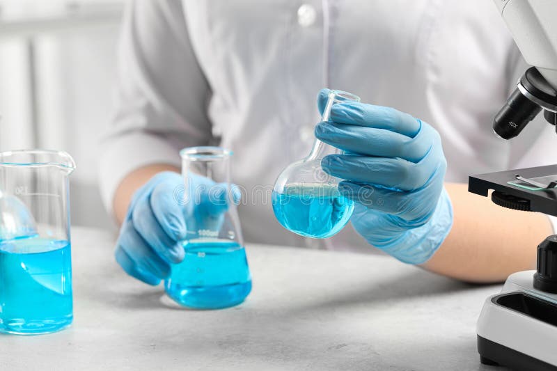 Scientist with Flasks of Light Blue Liquid at White Table in Laboratory ...