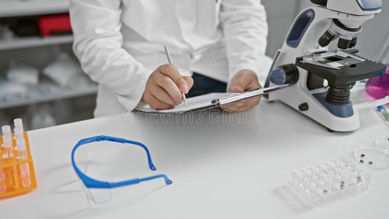 Scientist in Lab Coat Writing Notes with Microscope and Test Tubes in a ...