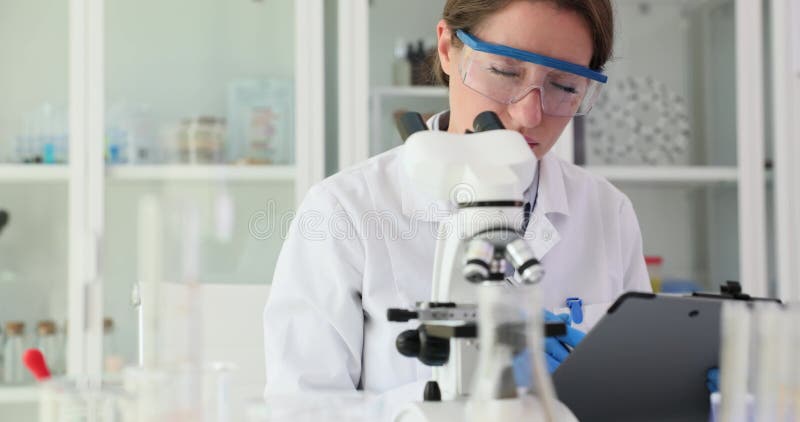 Scientist Looks through a Microscope and Writes Down Information about ...