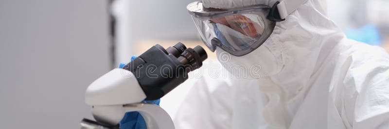 Scientist in Protective Suit and Mask Looks through Microscope Stock ...