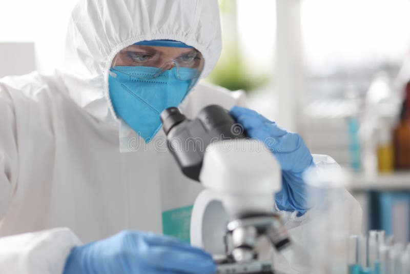 Scientist in Protective Suit and Respirator Looking through Microscope ...