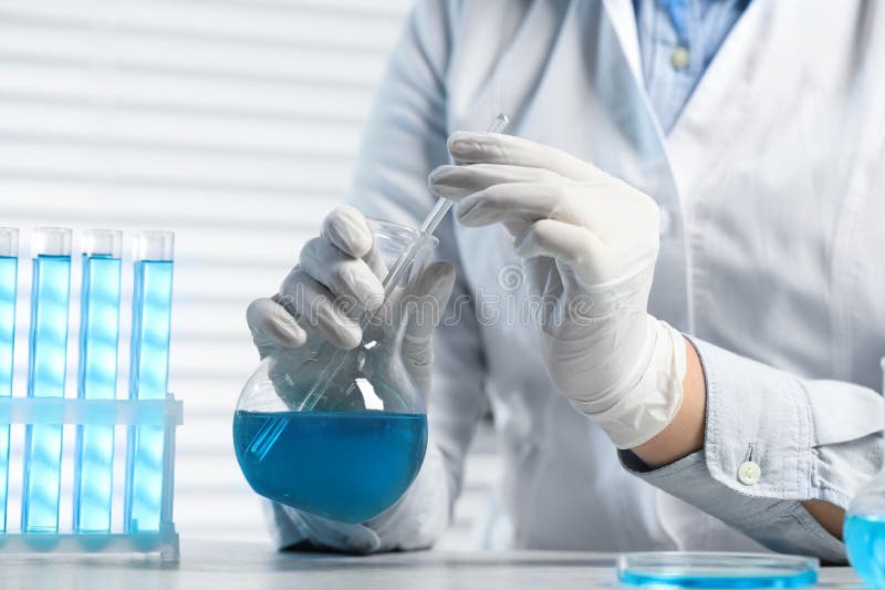 Scientist Taking Sample of Light Blue Liquid at White Table in ...