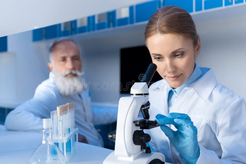 Scientist Using Microscope while Working in Lab with Colleague Behind ...