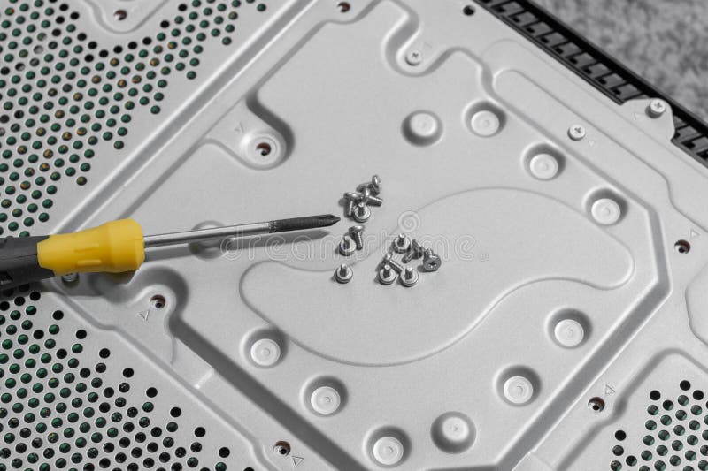 Screwdriver and Small Screws on Perforated Metal Cover. Electronic ...