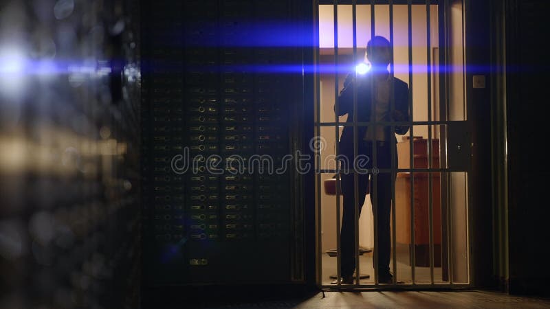 A Security Officer is Examining a Vault with a Flashlight at a Bank for ...