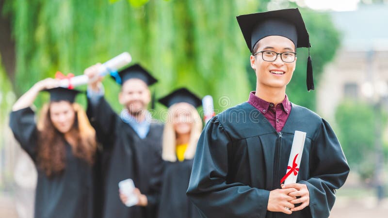 Selective Focus of Smiling Asian Graduate with Classmates Behind Stock ...