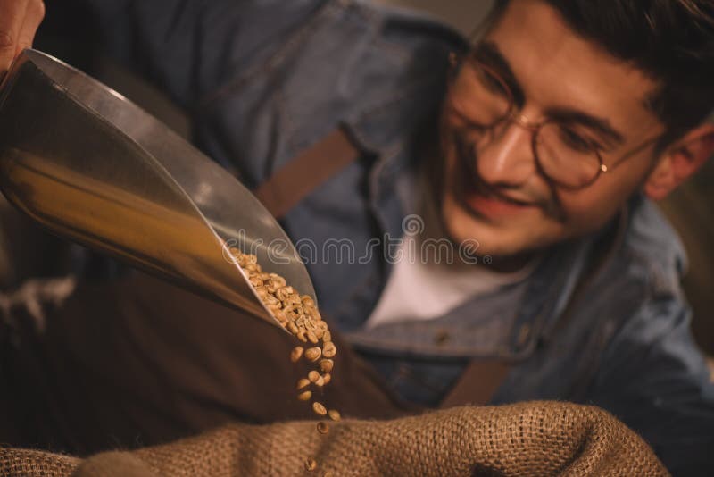 Selective Focus of Smiling Worker in Apron Pouring Coffee Beans into ...