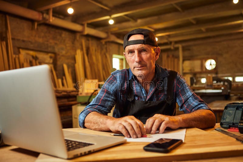 Senior Carpenter Works on the Computer and Look at the Camera in the ...