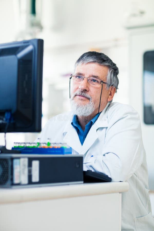 Serious Doctor Looking at Computer while Holding Clipboard at De Stock ...