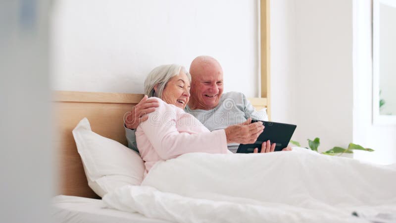 Senior Happy Couple And Together With Tablet In Bedroom With Embrace