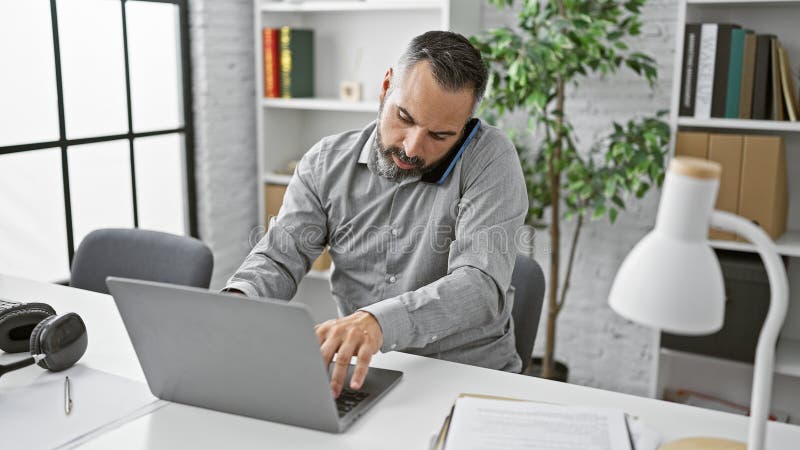 Senior Hispanic Man with Beard and Grey Hair Multitasking in a Modern ...