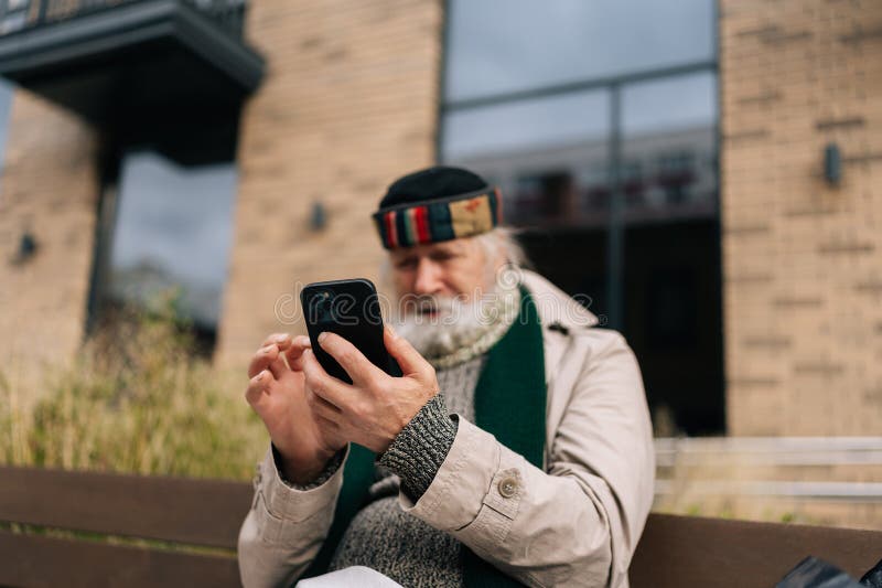 Senior Homeless Man Sitting on Urban Bench, Using Smartphone, Checking ...