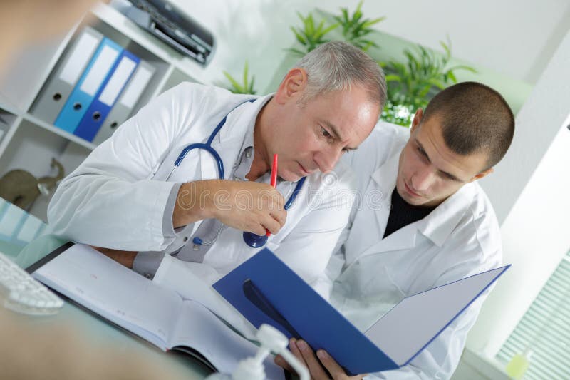Senior and Junior Male Doctors Looking at File Stock Image - Image of ...