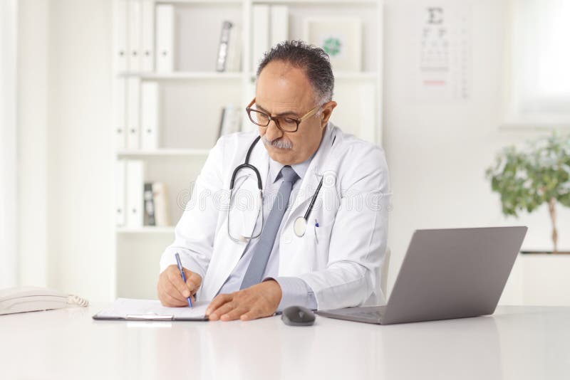 Senior Male Doctor Writing a Document in an Office and Sitting at a ...