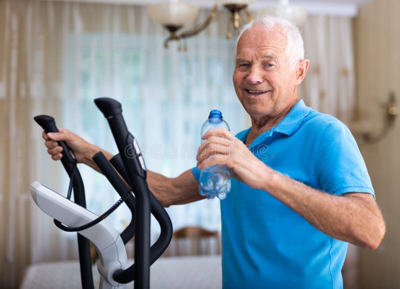 Senior Man with Bottle of Water Using Elliptical Trainer at Home Stock ...