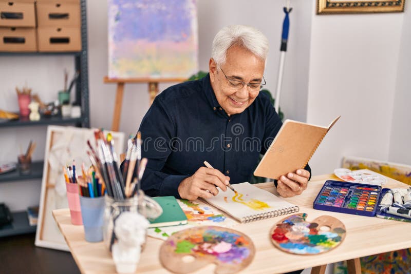 Senior Man Drawing on Notebook Reading Book at Art Studio Stock Image ...