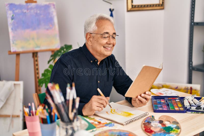 Senior Man Drawing on Notebook Reading Book at Art Studio Stock Photo ...