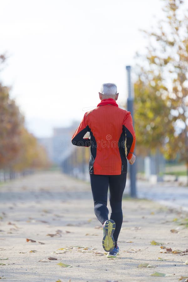 A Senior Man Dressed in Black and Orange is Running in the Park Stock ...