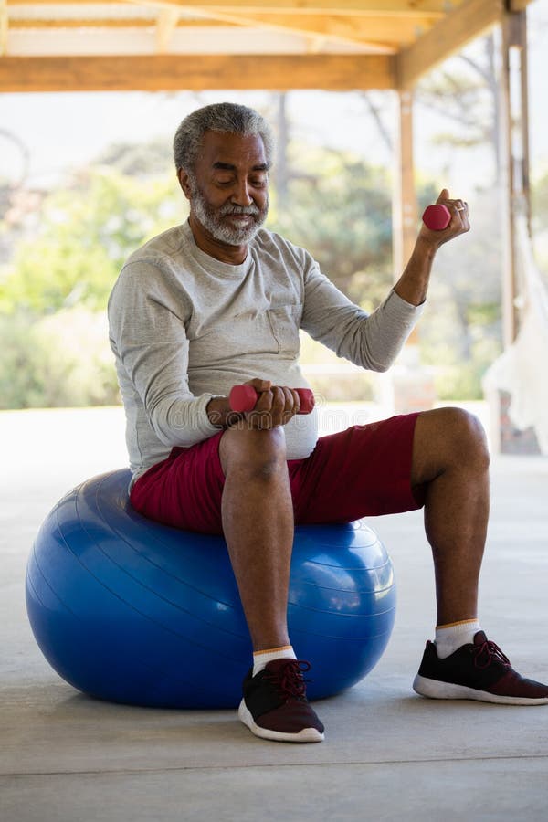 Senior Man Exercising with Dumbbells on Exercise Ball in the Porch ...