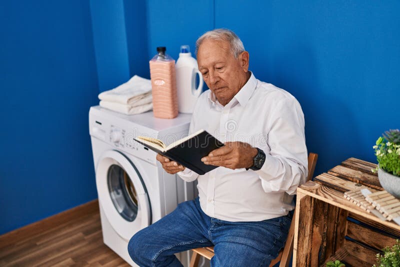 Senior Man Reading Book Waiting for Washing Machine at Laundry Room ...