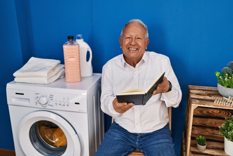 Senior Man Reading Book Waiting for Washing Machine at Laundry Room ...