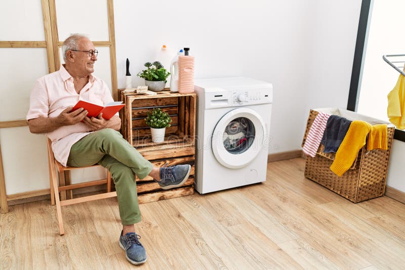 Senior Man Reading Book Waiting for Washing Machine at Laundry Room ...